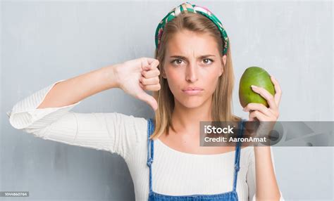 그런 지 위에 아름 다운 젊은 여자와 성 난 얼굴 아래로 엄지 싫어 보여주는 음수 부호 거부 개념 신선한 망고를 들고 벽 그레이 개념에 대한 스톡 사진 및 기타 이미지