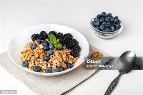 건강한 아침 식사 홈메이드 그래놀라 뮤즐리 블랙베리 블루베리 견과류 꿀 민트가 있는 시리얼을 흰색 바탕에 흰색 그릇에 담았습니다 0명에 대한 스톡 사진 및 기타 이미지