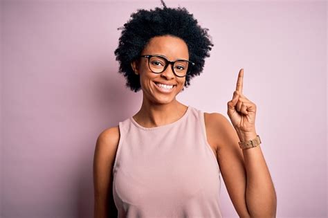 젊은 아름 다운 아프리카 계 미국인 Afro 여자 곱슬 머리 를 입고 티셔츠와 안경 을 입고 손가락을 가리키는 성공적인 아이디어 종료하고 행복 넘버 원 T 셔츠에 대한 스톡