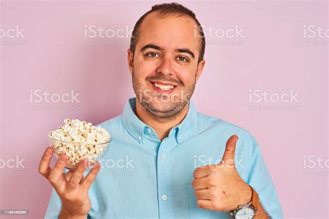 확인 기호를하고 큰 미소와 함께 행복 고립 된 분홍색 배경 위에 서 팝콘 그릇을 들고 젊은 남자 손가락으로 엄지 손가락 우수한 기호 개념에 대한 스톡 사진 및 기타 이미지