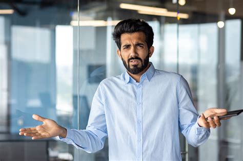 화가 난 젊은 인도 남성 사업가가 전화기를 손에 들고 사무실에 서서 손을 벌리고 카메라에 실망한 표정을 짓고 있다 20 24세에 대한 스톡 사진 및 기타 이미지 Istock