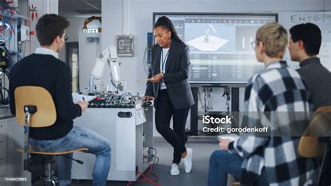 대학 로봇 수업 로봇 팔을 사용하는 학생들에게 공학을 설명하는 흑인 교사 로봇 손을 프로그래밍하는 젊은 엔지니어의 다양한 그룹 컴퓨터 과학 교육 빌드 디자인 배우기 교실에