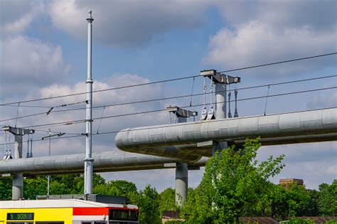 트램 선로 위를 가로지르는 대형 지역 난방 파이프라인 가공 전력선과 트램이 접근하고 있습니다 녹지로 둘러싸인 도시 기술 인프라 0명에 대한 스톡 사진 및 기타 이미지