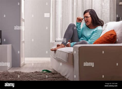 Barefoot Young Woman Sitting On A White Sofa In Her Living Room