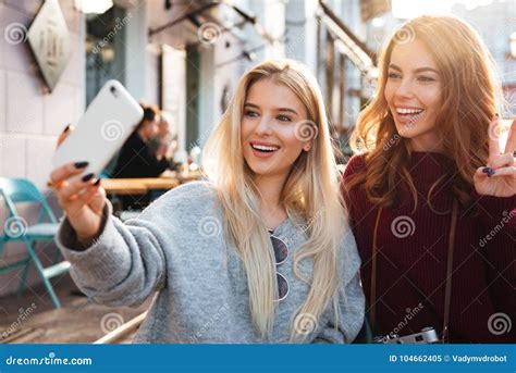 Two Happy Cheerful Girls Taking A Selfie While Sitting Together Stock
