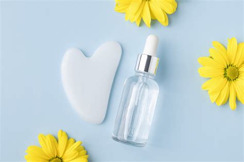 기름이 든 유리병 꽃이 있는 파란색 배경에 얼굴 마사지를 위한 Gua Sha 돌 화장품 얼굴 피부 관리 및 스파 자연 치료 개념입니다 개념에 대한 스톡 사진 및 기타 이미지