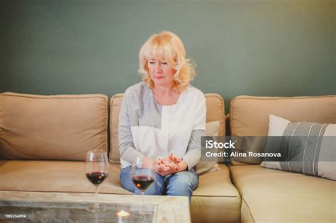 누군가를 기다리는 레드 와인 두 잔과 함께 소파에 앉아 있는 중년 금발 머리 슬픈 여자 외로움 싸움 축하 혼자 개념 가정 생활에