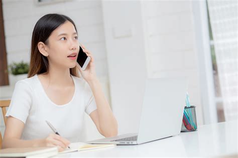 젊은 아시아 여성은 노트북 컴퓨터로 집에서 전화와 직장 노트북에 쓰고 스마트 폰에 말하기 집에 머물 가정 생활 비즈니스 및 통신 개념 가정 생활에 대한 스톡 사진 및 기타