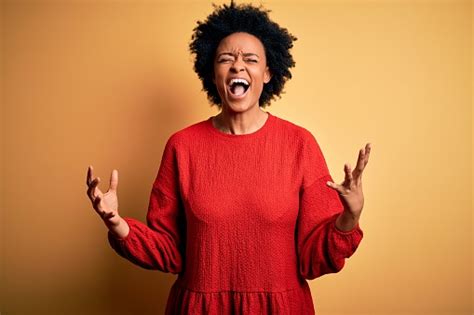 젊은 아름 다운 아프리카 계 미국인 Afro 여자 곱슬 머리 캐주얼 스웨터를 입고 미친 미친 소리와 공격적인 표정과 팔을 제기 고함 좌절 개념입니다 감정에 대한 스톡 사진