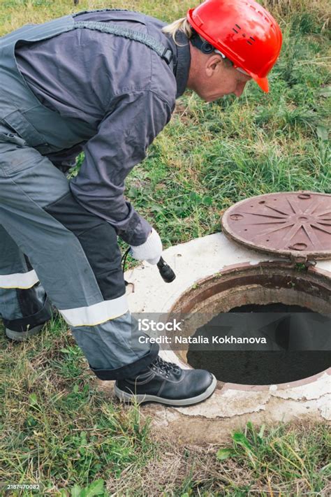 손전등이 달린 헬멧을 쓴 작업자가 열린 우물을 검사하고 있습니다 우물 정화조 계량기 및 파이프의 유지 보수 50 54세에 대한 스톡 사진 및 기타 이미지 Istock