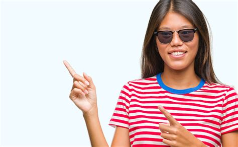 젊은 아시아 여자는 웃 고 옆에 두 손과 손가락으로 가리키는 카메라 보고 격리 된 배경 위에 선글라스를 착용 가리키기에 대한 스톡 사진 및 기타 이미지 Istock