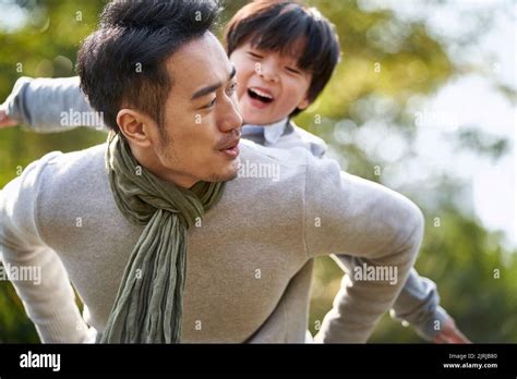 Young Asian Father Carrying Son On Back Having Fun Enjoying Nature