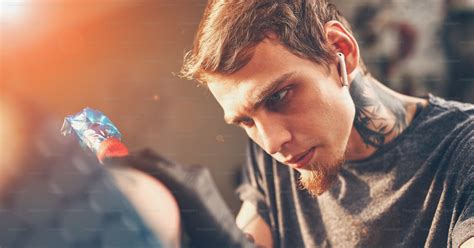 젊은 남자 문신 가게 회전식 문신 기계 검은 잉크 렌즈 플레어에서 소녀의 손에 문신을 때린다 사진 Unsplash의