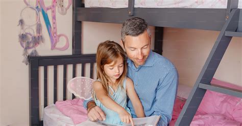 어린 딸 소녀에게 책을 읽는 아빠 침실의 침대에 앉아 있는 두 명의 행복한 가족 웃는 아버지와 아이는 집에서 함께 시간을