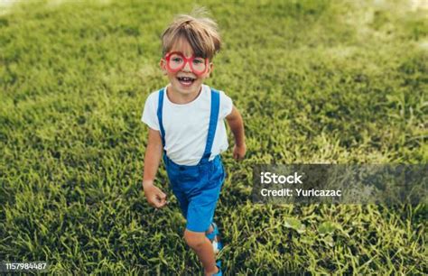 푸른 반바지 흰색 티셔츠와 자연 배경에서 재생 빨간 종이 안경을 입고 행복 한 어린 소년의 야외 이미지입니다 공원에서 녹색 잔디에서 실행 쾌활한 아이 아이가 재미있어요 T