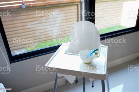 집안의 창문 옆에 흰색 높은 의자를 닫고 파란색 숟가락이있는 빈 흰색 그릇이 유아 식사 아기 먹이 개념을 위해 준비됩니다 건강관리와 의술에 대한 스톡 사진 및 기타 이미지
