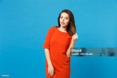 아름 다운 갈색 머리 젊은 여 자가 레드 오렌지 드레스를 입고 카메라 서 있는 포즈 유행 블루 벽 배경 스튜디오 초상화에 고립 사람들의 라이프 스타일 패션 컨셉 복사 공간을