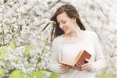 편안한 미소 영 부드러운 여자 시 정원이 나 공원 피 나무 배경에 흥미로운 책 서를 읽고 가벼운 캐주얼 옷에 봄 자연 꽃입니다 라이프 스타일 레저 개념 고름에 대한 스톡