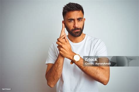 고립 된 흰색 배경 위에 서있는 티셔츠를 입은 젊은 인도 남자손 제스처로 상징적 인 총을 들고 살인 사격 무기 화가 난 얼굴 T 셔츠에 대한 스톡 사진 및 기타 이미지