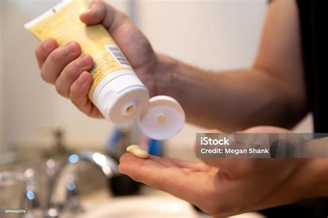 젊은 백인 손에 쥐 어 튜브 적용 여드름 얼굴 세척 로션 스킨 케어 제품 닫기 최대 및 확대 집 욕실 싱크 및 퍼스널 케어 위생과 청결에 대 한 거울에 남자에 대한 스톡