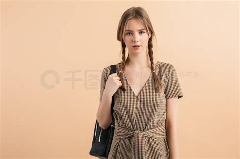 摆姿势高清图片 年轻漂亮的女士穿着花呢连衣裙留着两条辫子肩上背着黑色背包在米色背景下梦幻般地看着镜头 产品实拍免费下载 jpg格式 编号 千图网