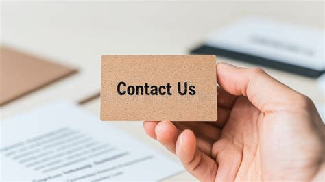 A Hand Holding A Contact Card Displaying Contact Us Surrounded By Business Documents For