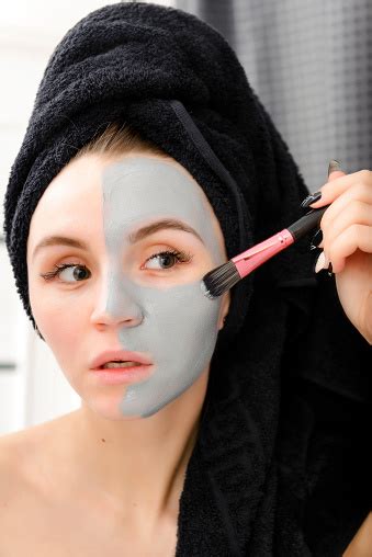 머리에 검은 수건을 가진 백인 여성이 거울 앞에서 브러시로 얼굴에 마스크를 놓습니다 20 24세에 대한 스톡 사진 및 기타