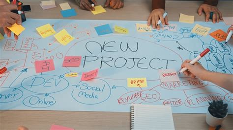 나무 테이블 Sactr의 큰 계획 시트를 중심으로 협업하는 다채로운 스티커 메모와 손으로 새 프로젝트를 개발하기 위한 창의적인 브레인스토밍 세션 가계에 대한 스톡 사진 및