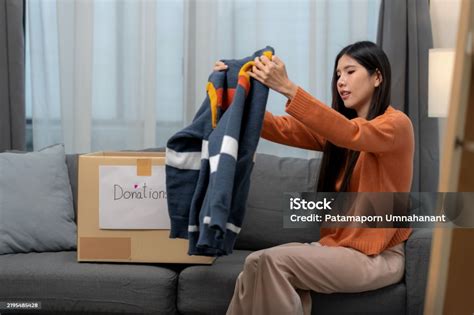 집에서 옷으로 가득 찬 기부 상자를 준비하는 공감하는 아시아 여성 자선 활동 재활용 및 지역 사회 봉사 활동을 촉진합니다 비영리 단체에 대한 보살핌과 지원의 즐거운 순간