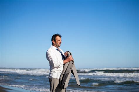 느슨한 흰색 셔츠 블루 넥타이와 그의 어깨에 또는 손에 바다 파도와 함께 해변에 서 있는 중 년 기업 남자의 상체는 배경에서 고독 개념에 대한 스톡 사진 및 기타 이미지