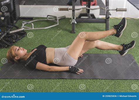A Young Asian Woman Does Flutter Kicks While Lying On A Black Mat At