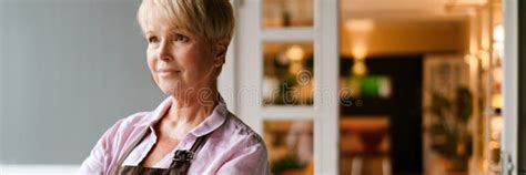 Mature Woman Wearing Apron Looking Aside While Standing In Cafe Stock