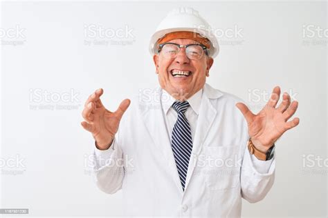 외투와 헬멧을 쓰고 있는 선임 회색 머리의 엔지니어 남자가 팔을 들고 눈을 감고 흥분을 일으키며 성공을 축하하는 고립된 흰색