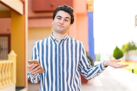Jeune Bel Homme Utilisant Un T L Phone Portable L Ext Rieur Faisant Un Geste De Doute Tout En
