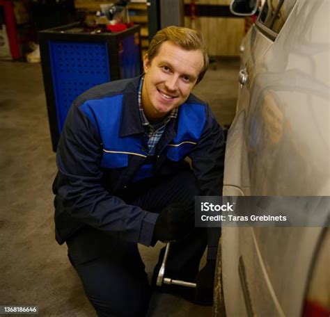 잘 생긴 백인 남자 전문 자동차 정비사는 수동으로 렌치와 너트와 볼트를 풀고 수리 가게에서 카메라에 미소 자동차의 바퀴를 변경