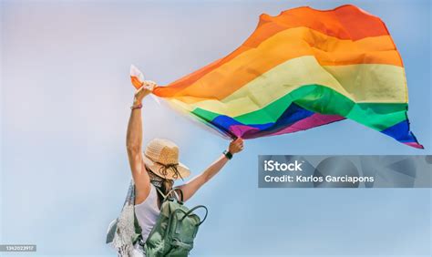 모자를 쓴 한 여성이 푸른 하늘에 대한 자부심 깃발을 들고 있다 자유와 관용의 개념 Lgtb 50 54세에 대한 스톡 사진 및 기타 이미지 Istock