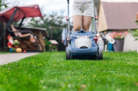 잔디 깎는 기계를 사용하여 정원에서 잔디를 자르는 사람 잔디 깎는 기계는 큰 바퀴가 달린 견고한 디자인을 가지고 있으며 앞으로