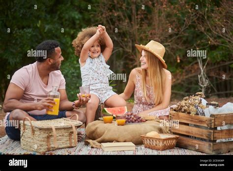 Loving ethnic dad pouring natural orange juice into glass during picnic ...