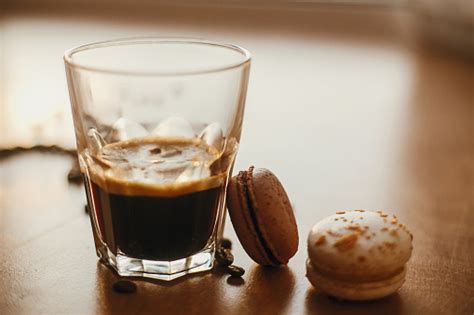 따뜻한 빛의 나무 테이블에 향기로운 볶은 커피 콩과 마카롱유리 컵에 거품뜨거운 에스프레소 대체 커피 양조 개념입니다 복사 공간 가루로 빻은에 대한 스톡 사진 및 기타 이미지