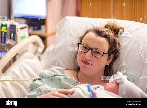 Happy And Tired New Mom Holding Newborn Baby In Hospital Bed After