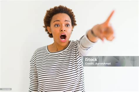 젊은 아름 다운 아프리카계 미국인 여자 흰색 배경 위에 줄무늬 스웨터를 입고 앞에 놀란 손가락으로 오픈 입 깜짝 표현 앞에 뭔가