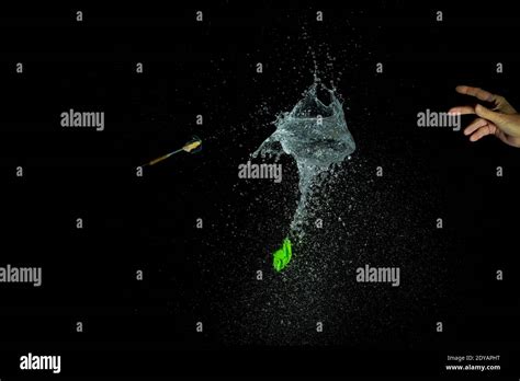 a high speed image of a thrown dart hitting a water balloon and
