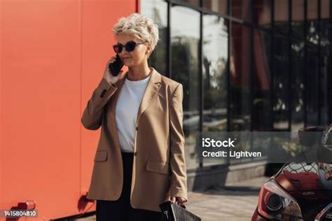 서류 가방을 손에 들고 고급 자동차 근처에서 전화로 이야기하는 세련된 비즈니스 여성 Brand Name Smart Phone에 대한 스톡 사진 및 기타 이미지 Brand