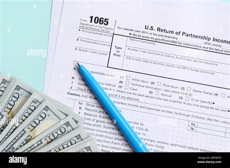 1065 Tax Form Lies Near Hundred Dollar Bills And Blue Pen On A Light