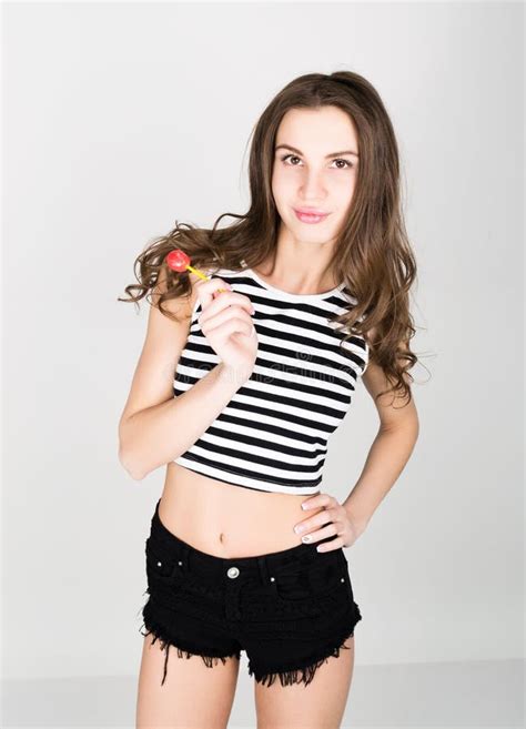 Bella Ragazza Esile Negli Shorts Neri Ed In Una Cima A Strisce Mangiante Caramella Labbro Del