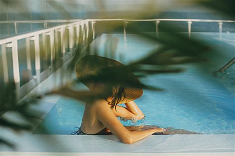 야자수 잎 아래 수영장에서 휴식을 취하고 여름 휴가에 따뜻한 햇볕이 잘 드는 빛을 즐기는 모자를 쓴 세련된 젊은 여성 고급 열대 리조트에서 휴가에 선햇에 소녀 옥상수영장에서