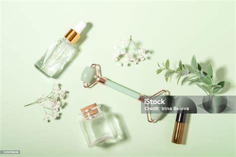녹색 옥 롤러 얼굴 마사지 기 구아슈 유리 화장품 병과 흰색 꽃과 밝은 녹색 배경에 홈 스파 케어 아름다움과 젊음 안티 에이지의 개념 상단 보기 플랫 레이 괄사에 대한 스톡