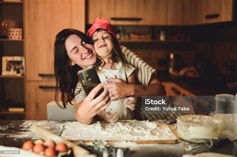 함께 요리하는 동안 핸드폰으로 셀카를 찍는 가족 부엌에서 딸과 셀카를 찍는 행복한 젊은 어머니 웃는 어머니와 딸이 집에서 요리하는 동안 셀카 만들기 수제 케이크 요리 전업