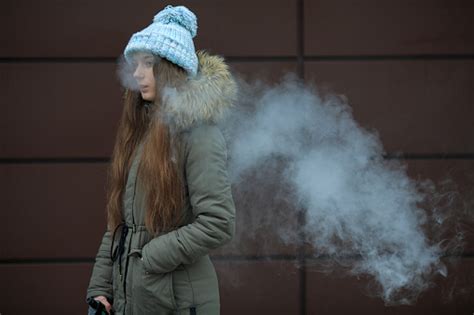 Vape 십 대 젊은 예쁜 백인 소녀 겨울에 거리에 현대 갈색 배경 맞은편 전자 담배를 흡연 아이에 대한 스톡 사진 및 기타 이미지 Istock
