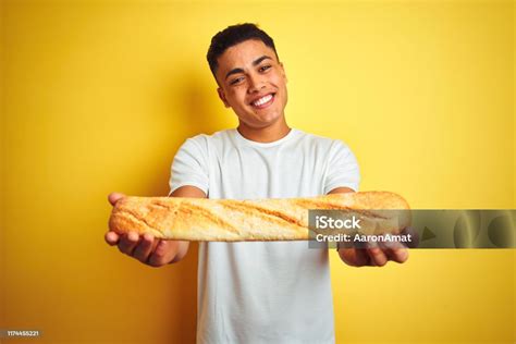 고립된 노란색 배경 위에 빵을 들고 있는 젊은 브라질 제빵사 남자가 행복한 얼굴을 하고 이빨을 보여주는 자신감 있는 미소로 미소짓고 있습니다 건강한 생활방식에 대한 스톡